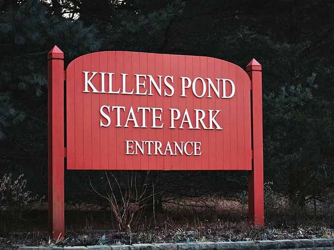 The classic red entrance sign stands like a cheerful gatekeeper, promising adventures that GPS directions simply can't prepare you for.
