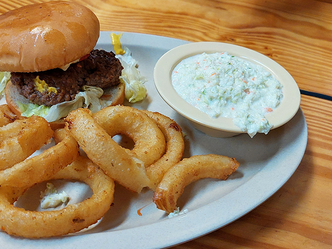 That perfect trio—juicy burger, crispy onion rings, and creamy coleslaw—a holy trinity of comfort that makes Monday feel like Saturday.