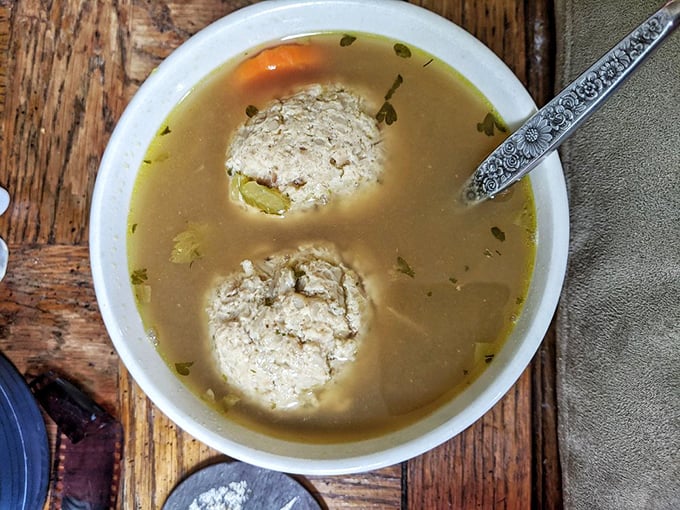 Behold the matzo ball soup in all its glory—two perfectly fluffy dumplings swimming in golden broth that's clearly been simmering since before your morning alarm went off.