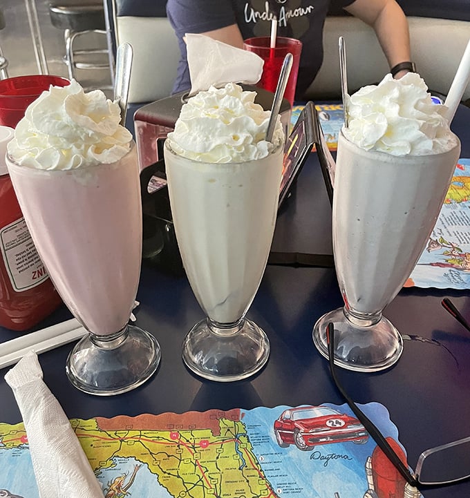 Three milkshakes standing at attention like creamy soldiers ready for duty. The whipped cream mountains on top require their own zip code.