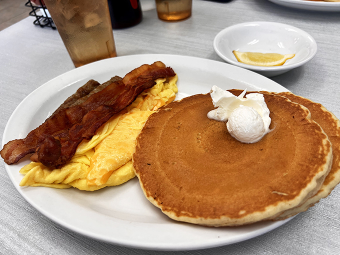 Breakfast nirvana achieved: golden pancakes with a perfect dollop of whipped butter, scrambled eggs that defy physics, and bacon that should win awards.