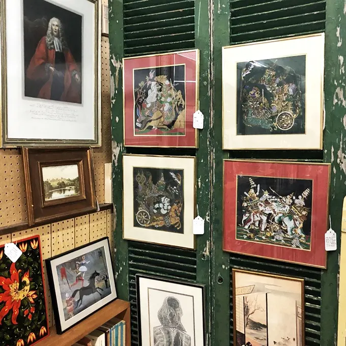 Art displayed on weathered green shutters—a gallery within a gallery. These frames hold memories that outlasted their original owners.