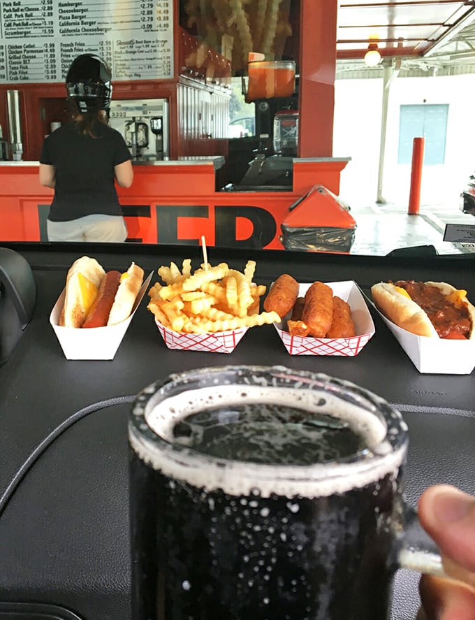 Car dining at its finest—hot dogs, fries, and that legendary root beer creating the perfect dashboard picnic. Who needs a fancy table when you've got a steering wheel?