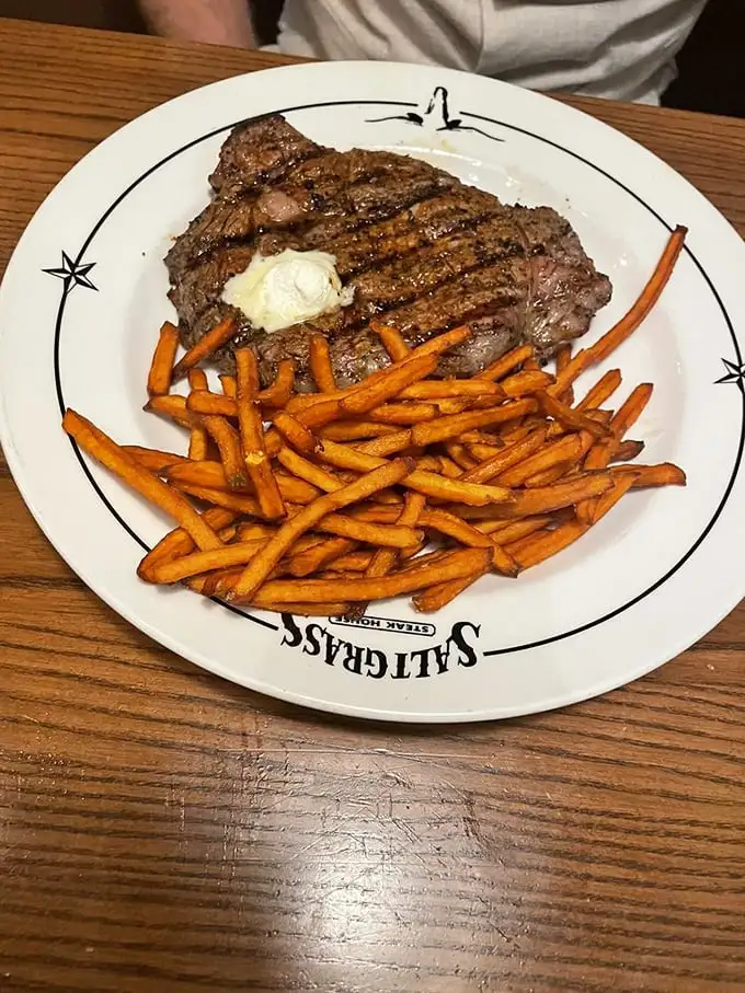 A perfectly grilled steak topped with butter meets sweet potato fries. This plate isn't just dinner—it's what food dreams are made of.