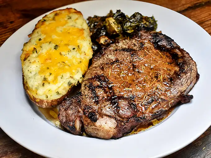 A perfectly charred ribeye alongside a loaded baked potato that's practically wearing a cheese tuxedo. Simple perfection on a plate.