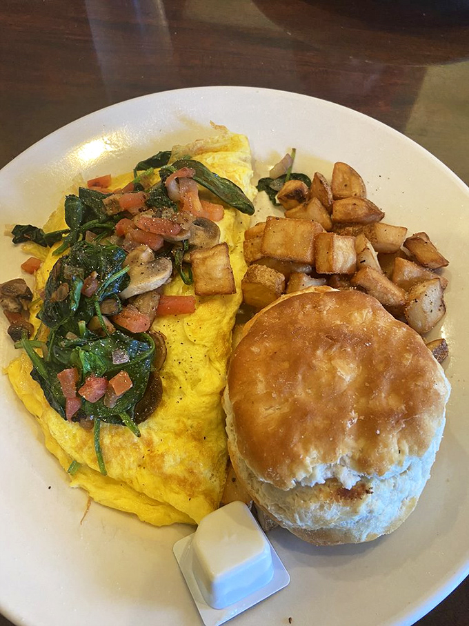 This isn't just an omelet—it's a vegetable garden wrapped in fluffy egg blanket, escorted by golden hash browns and a biscuit worthy of its own fan club.