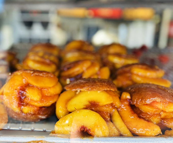 Summer in a donut—golden peach slices nestled in glazed dough create the kind of seasonal magic that makes waiting in line worthwhile.