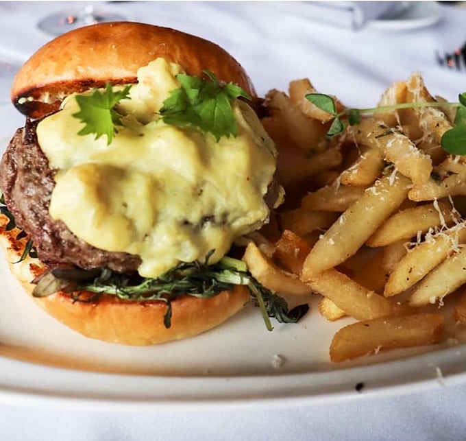 This isn't just a burger—it's architecture. The golden crown of what appears to be béarnaise sauce transforms an everyday sandwich into weekend-worthy indulgence.