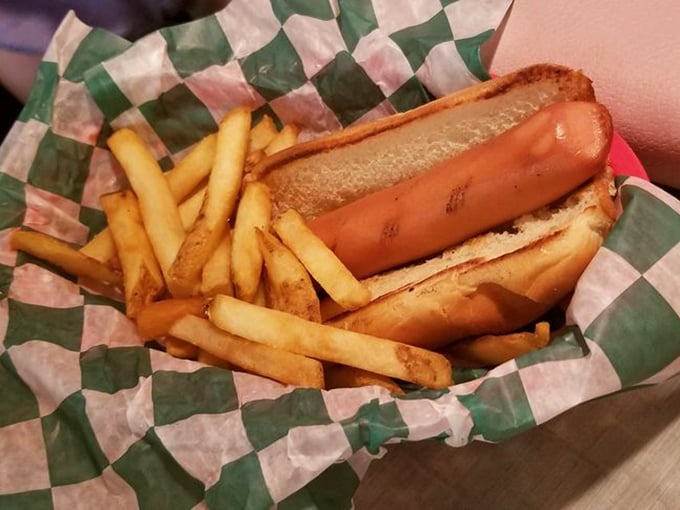 The classic American childhood on a checkered paper—a perfectly grilled hot dog nestled in a soft bun with golden fries standing at attention alongside.