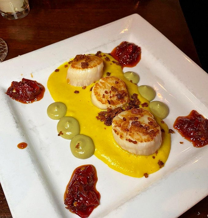 These seared scallops aren't just dinner—they're edible jewels from the Atlantic, served on a golden sauce canvas with artistic splashes of tomato jam.