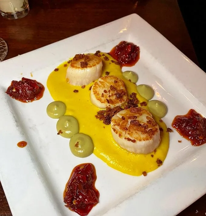 These seared scallops aren't just dinner—they're edible jewels from the Atlantic, served on a golden sauce canvas with artistic splashes of tomato jam.