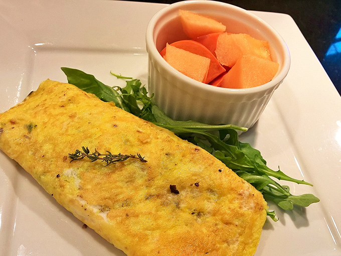 Breakfast perfection on a plate: A golden omelet nestled alongside fresh greens and sweet cantaloupe – simple, flawless execution to start your day.