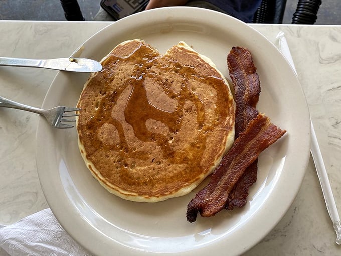 Breakfast's greatest hits album on a single plate—pancakes glistening with syrup and bacon so perfect it should come with its own theme music.