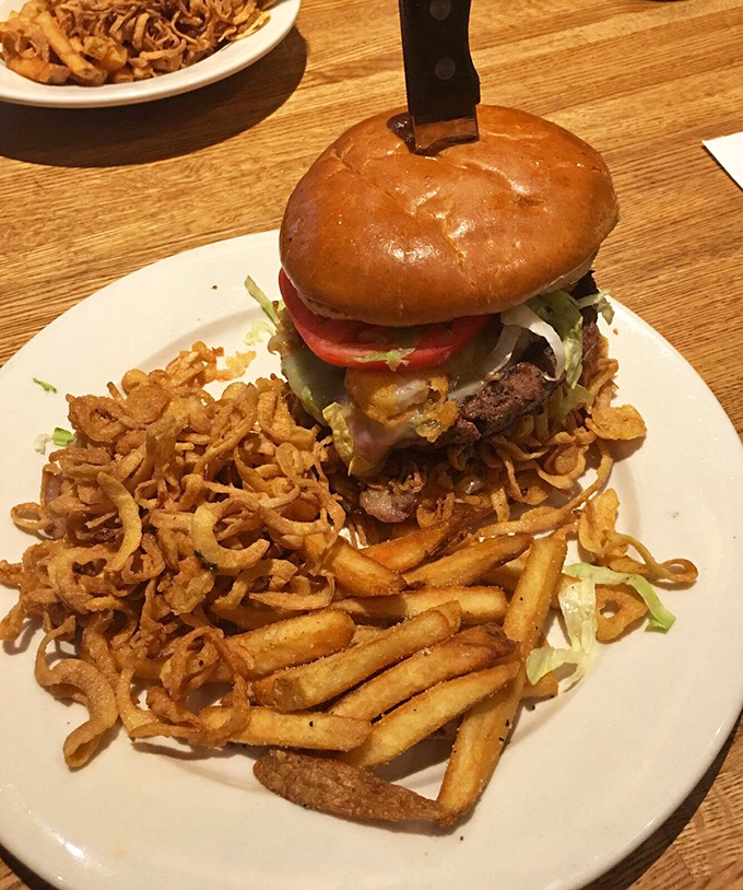 This isn't just a burger—it's a towering monument to American excess, complete with crispy onion strings that should be classified as addictive substances.