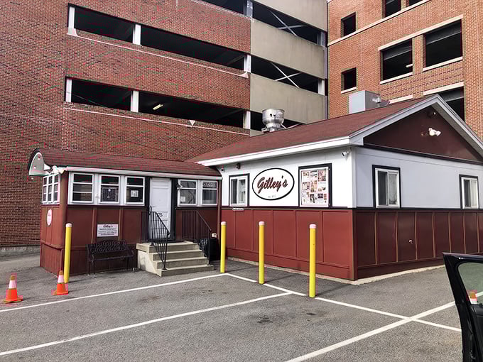 A humble red and white diner nestled against a parking garage—proof that culinary treasures often hide in plain sight.