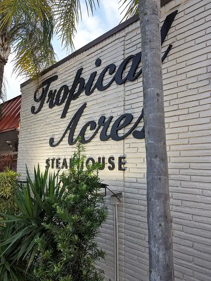 The iconic white brick façade of Tropical Acres glows invitingly at night, palm trees standing guard like old friends welcoming you home.