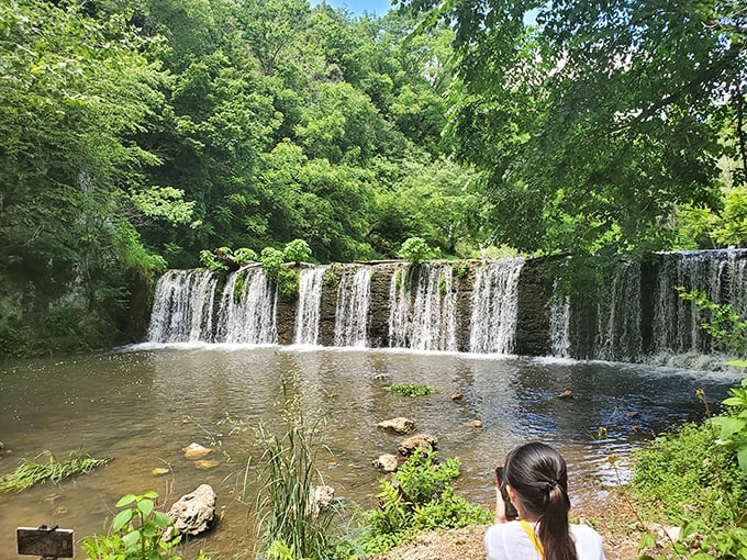 Nature's perfect curtain call – water cascades over a wide ledge, creating a serene backdrop that makes even smartphone photographers look like Ansel Adams.