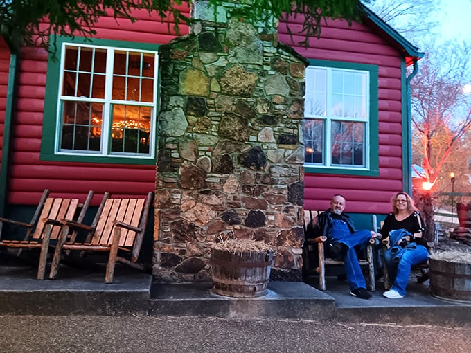 The crimson log cabin emerges from lush Ozark greenery like a storybook setting—complete with stone chimney and verdant landscaping that whispers "come on in."