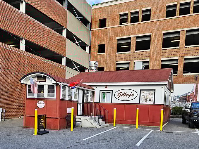 A humble red and white diner nestled against a parking garage—proof that culinary treasures often hide in plain sight.