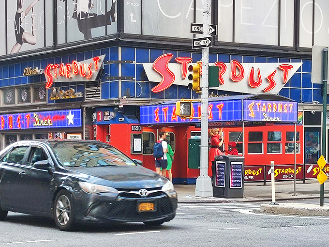 The neon-lit entrance to Ellen's Stardust Diner stands out like a Broadway marquee, promising both sustenance and showmanship in the heart of Times Square.