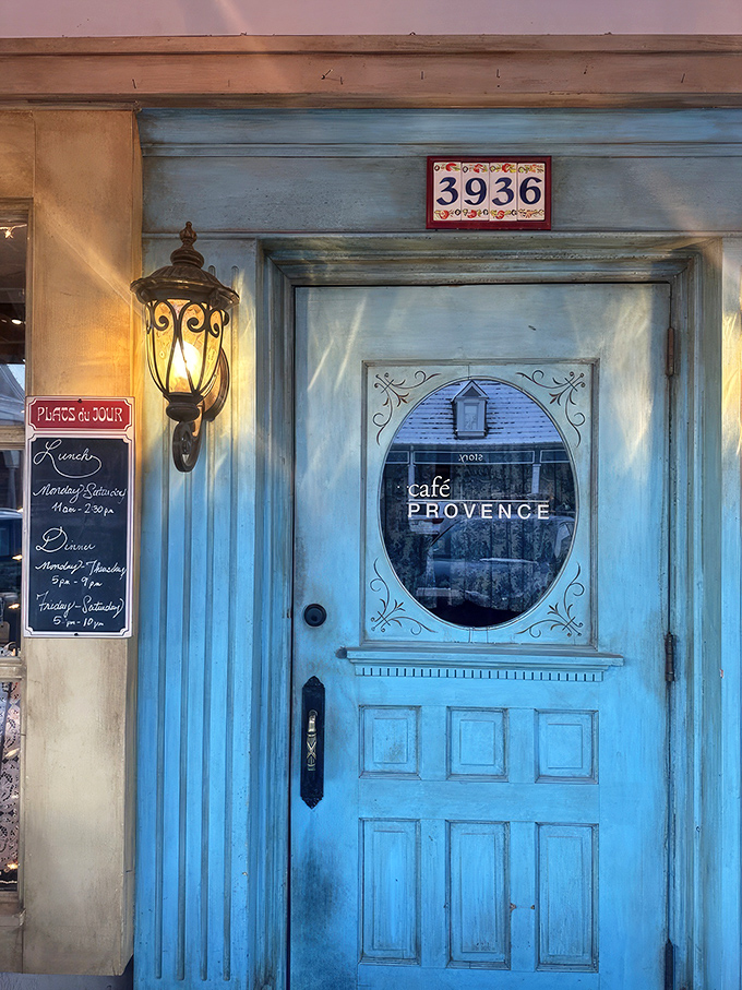 The iconic blue door of Café Provence beckons like a portal to southern France, complete with charming oval window and vintage lantern. Step through and prepare for culinary time travel.