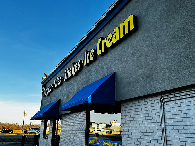 The humble roadside palace where burger dreams come true. Blue awnings and bright yellow signage beckon hungry travelers like a culinary lighthouse.