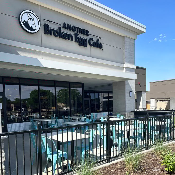 The modern facade of Another Broken Egg Cafe welcomes hungry patrons with its signature teal patio furniture—a breakfast beacon in Prairie Village.