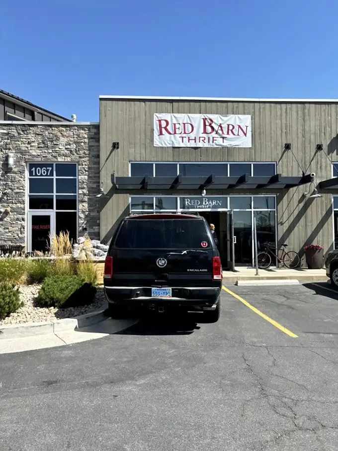 The iconic Red Barn Thrift stands proudly against Utah's mountain backdrop, colorful umbrellas inviting treasure hunters to step inside this Farmington gem.