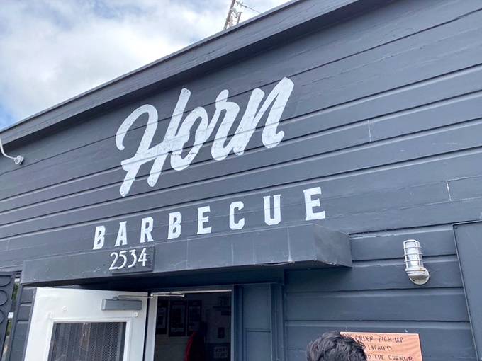 The unassuming exterior of Horn BBQ in Oakland – where that bold white lettering against dark panels is the architectural equivalent of a whisper about the best-kept secret in town.