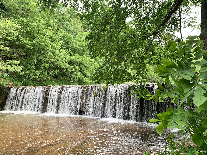 Nature's perfect curtain call – water cascades over a wide ledge, creating a serene backdrop that makes even smartphone photographers look like Ansel Adams.