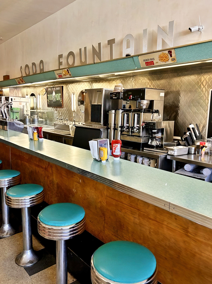 The soda fountain counter—where strangers become neighbors and diet plans go to die in the most glorious way possible.