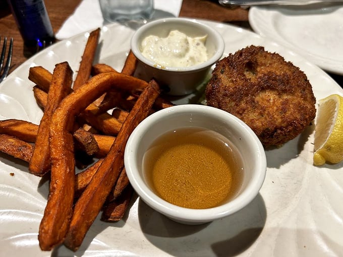 The crab cake's crispy exterior guards its treasure like a delicious bouncer, while sweet potato fries stand ready for their supporting role.
