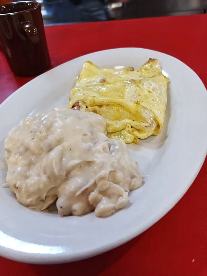 A plate where biscuits swim happily in creamy gravy alongside a perfectly folded omelet – comfort food that speaks the universal language of "mmmmm."