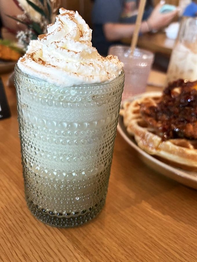 Whipped cream mountain meets textured glass—this isn't just a drink, it's a morning celebration with a waffle cameo in the background.