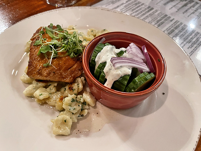 Salmon perched atop spätzle like it's posing for a food magazine, with a side of cucumber salad dressed for the occasion.