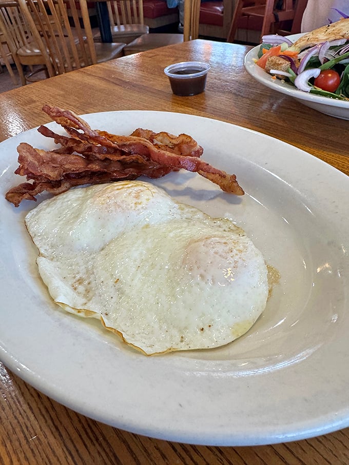 Sunny-side up eggs with perfectly crisped bacon—breakfast in its purest form. The kind of plate that reminds you why morning meals deserve our respect.