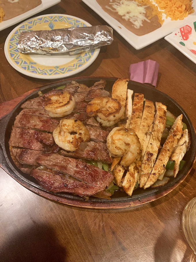 The fajita trinity—chicken, steak, and shrimp—arranged on a sizzling platter that announces its arrival before you even see it. Dinner and drama in one package.