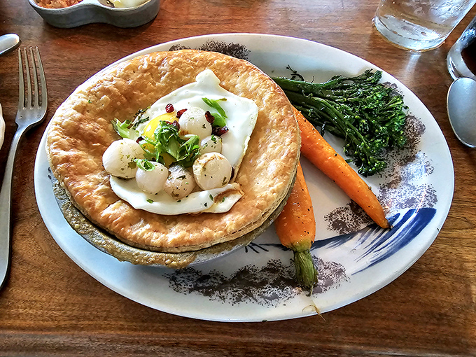 The Onion Pye arrives like a colonial surprise—a golden pastry crown revealing delicate scallops nestled in creamy sauce, with vegetables standing at attention.