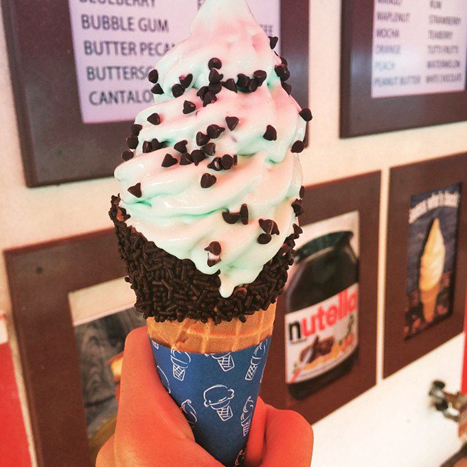 Mint and pink swirled soft serve dipped in chocolate sprinkles—wearing a blue paper collar like it's dressed for a fancy occasion.
