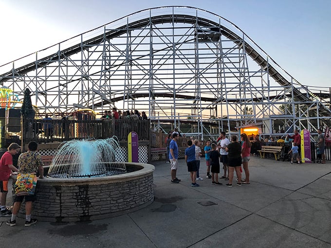 As dusk approaches, visitors gather near the fountain, planning their next ride while the coaster's silhouette creates a perfect backdrop for summer memories.