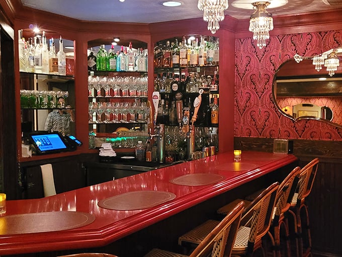 The bar at L'Auberge doesn't just serve drinks—it serves atmosphere. That rich red counter has probably heard more dinner plans and declarations of love than a romance novelist.