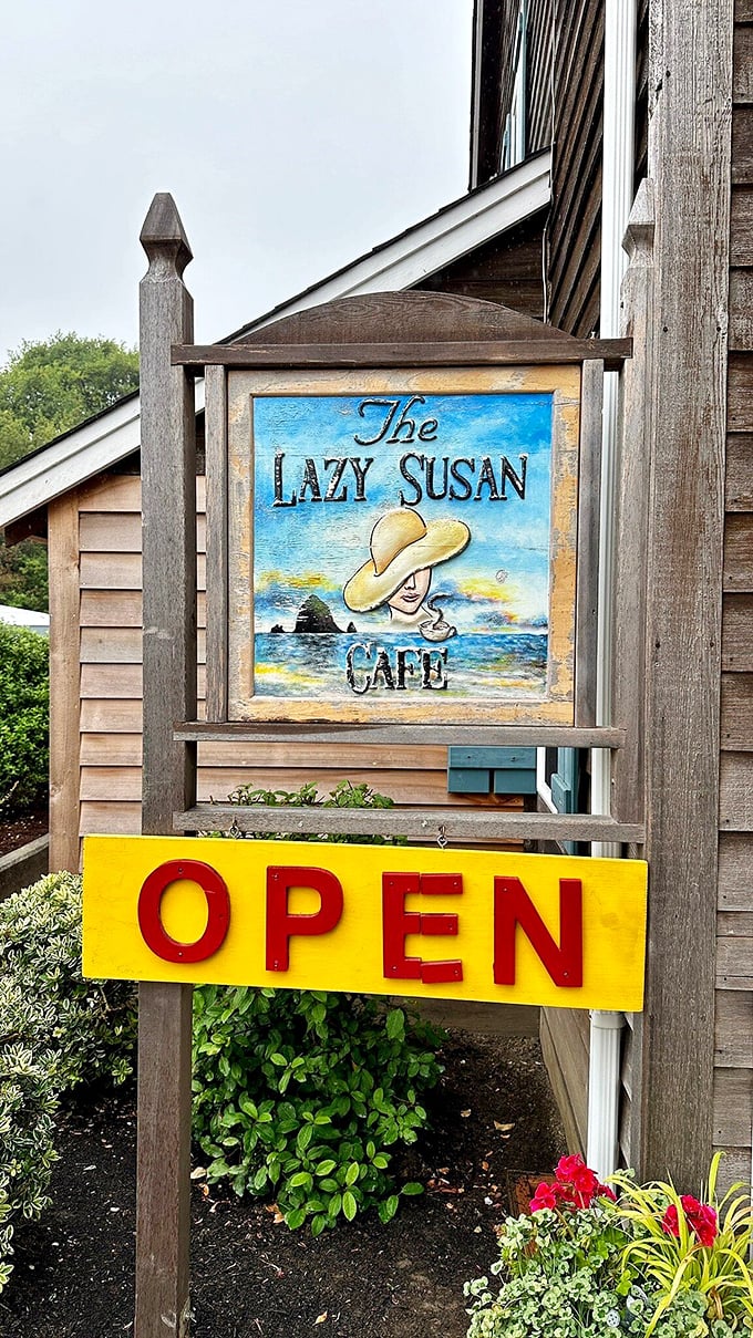 The painted sign featuring Haystack Rock and a sun-hatted figure promises coastal charm and relaxation. Yellow "OPEN" never looked so inviting.