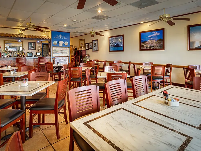 Warm wooden chairs and marble-topped tables create an inviting atmosphere, while framed images of Greek landscapes transport you across the Atlantic.