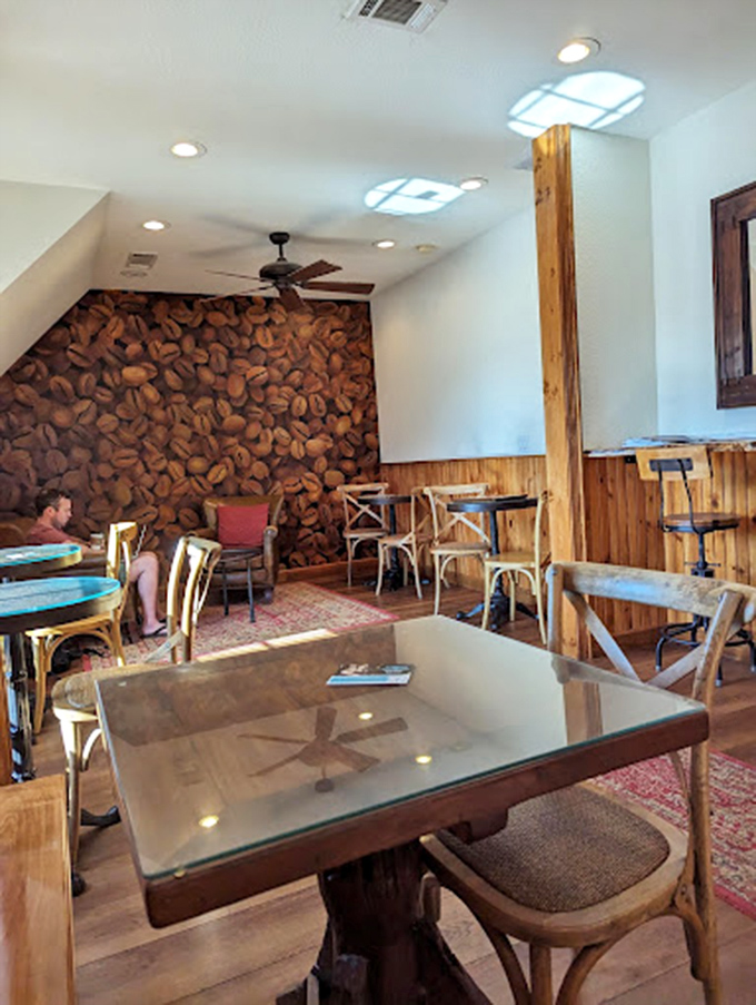 Coffee bean wallpaper that doesn't just decorate—it announces a mission statement. This cozy corner with wooden accents and glass-topped tables is where caffeine dreams come true.