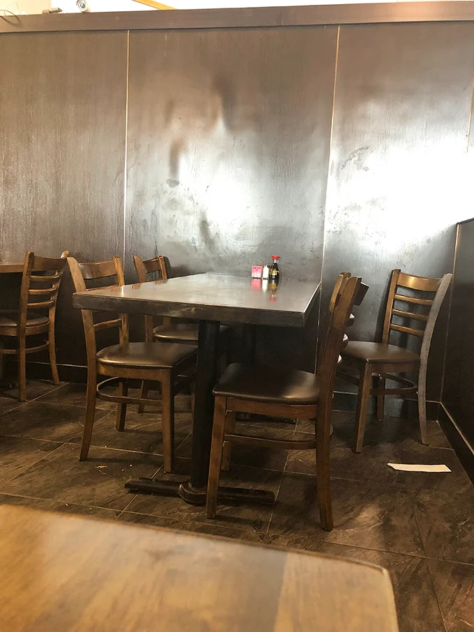 Simple wooden chairs and metallic walls create an unpretentious dining space where the focus remains squarely where it belongs—on your soon-to-be-overloaded plate.