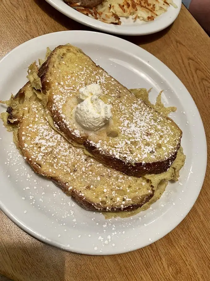 The French toast arrives like a powdered sugar snowfall on golden-brown perfection. That dollop of whipped cream isn't garnish—it's essential architecture.