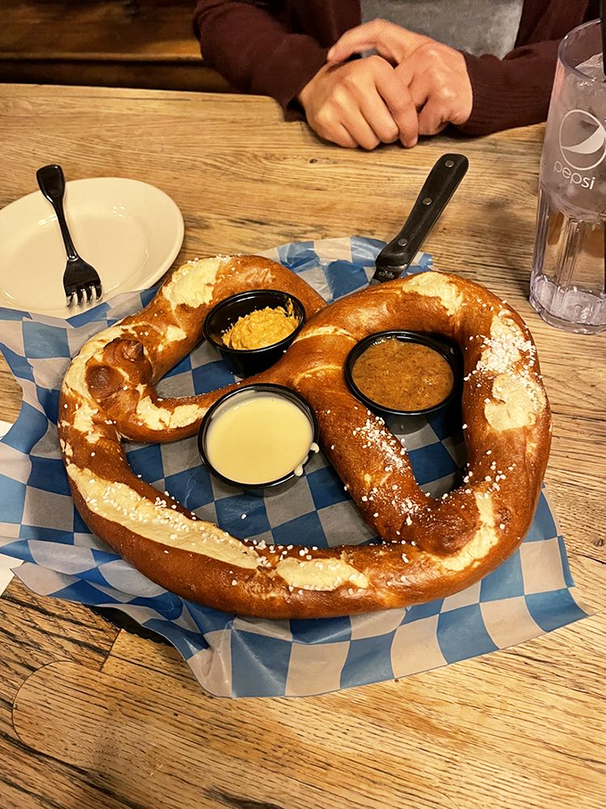 This pretzel isn't just big—it's the Schwarzenegger of baked goods, flexing its golden-brown muscles alongside three perfect dipping companions.