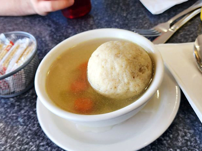 Golden broth cradling a perfect matzo ball – this isn't just soup, it's liquid sunshine with a dumpling island of joy.