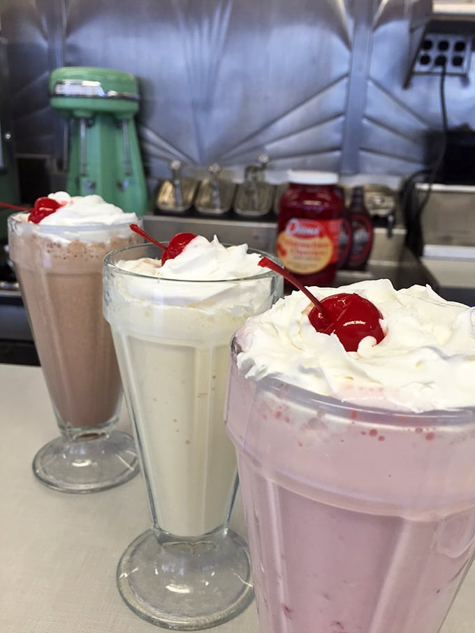 Three milkshakes standing at attention, topped with whipped cream mountains and cherry beacons. Resistance is futile, and frankly, unnecessary.