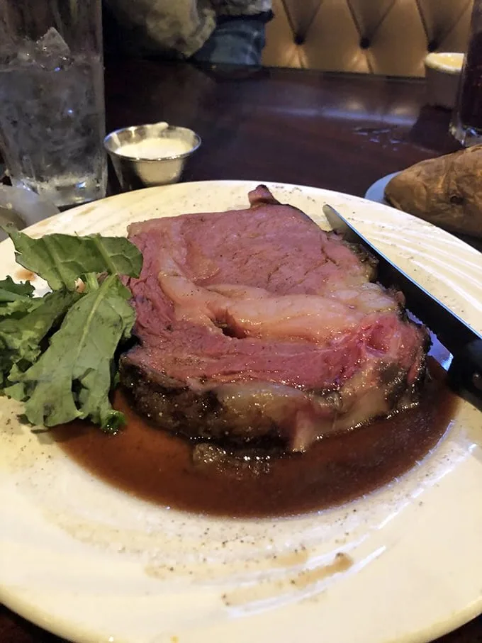 The prime rib doesn't just sit on the plate—it commands attention, a glistening monument to beef perfection surrounded by a moat of savory au jus.